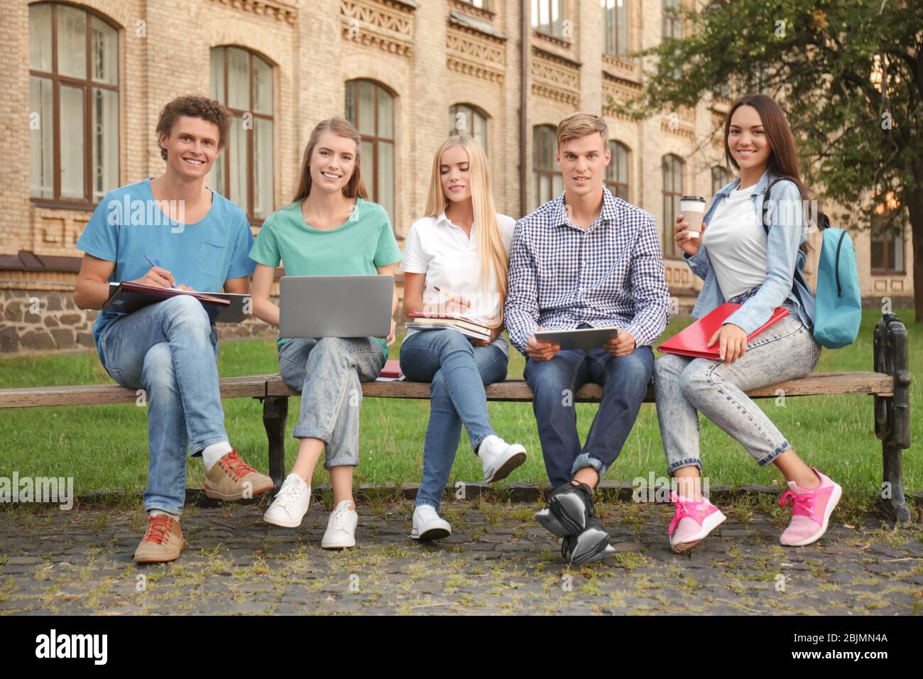 Group of young students sitting on bench near university building Stock ...