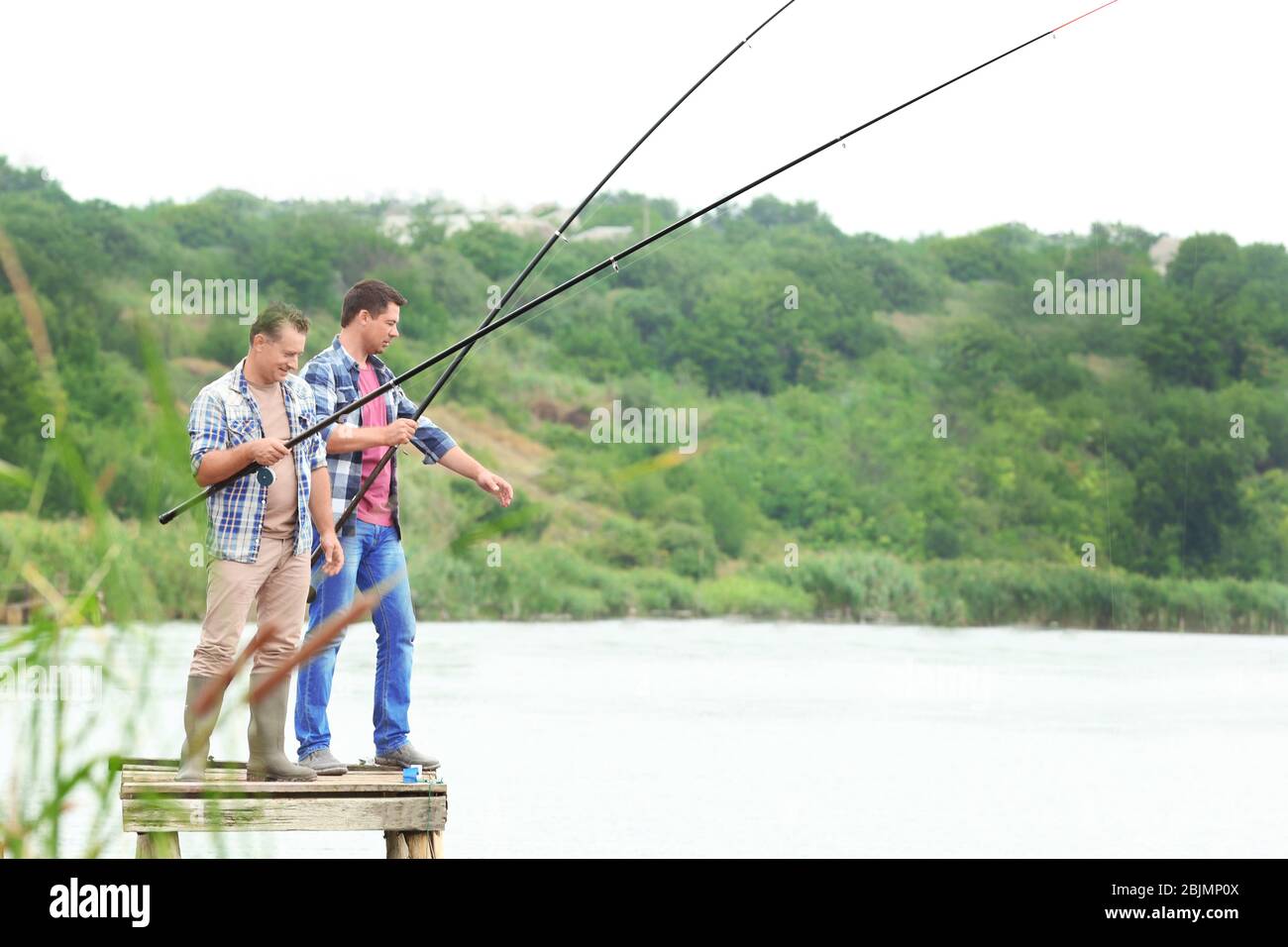 Two men fishing from pier on river Stock Photo - Alamy