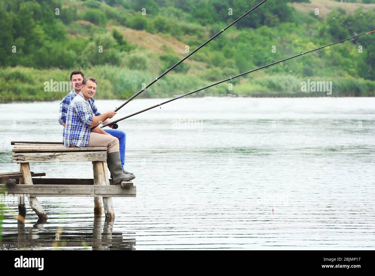 Two men fishing from pier on river Stock Photo - Alamy