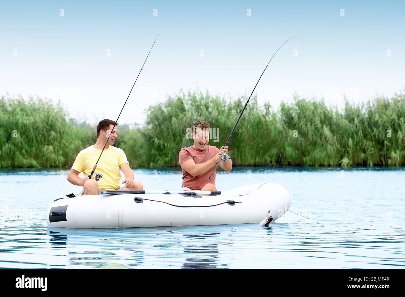 Two men fishing from inflatable boat on river Stock Photo - Alamy