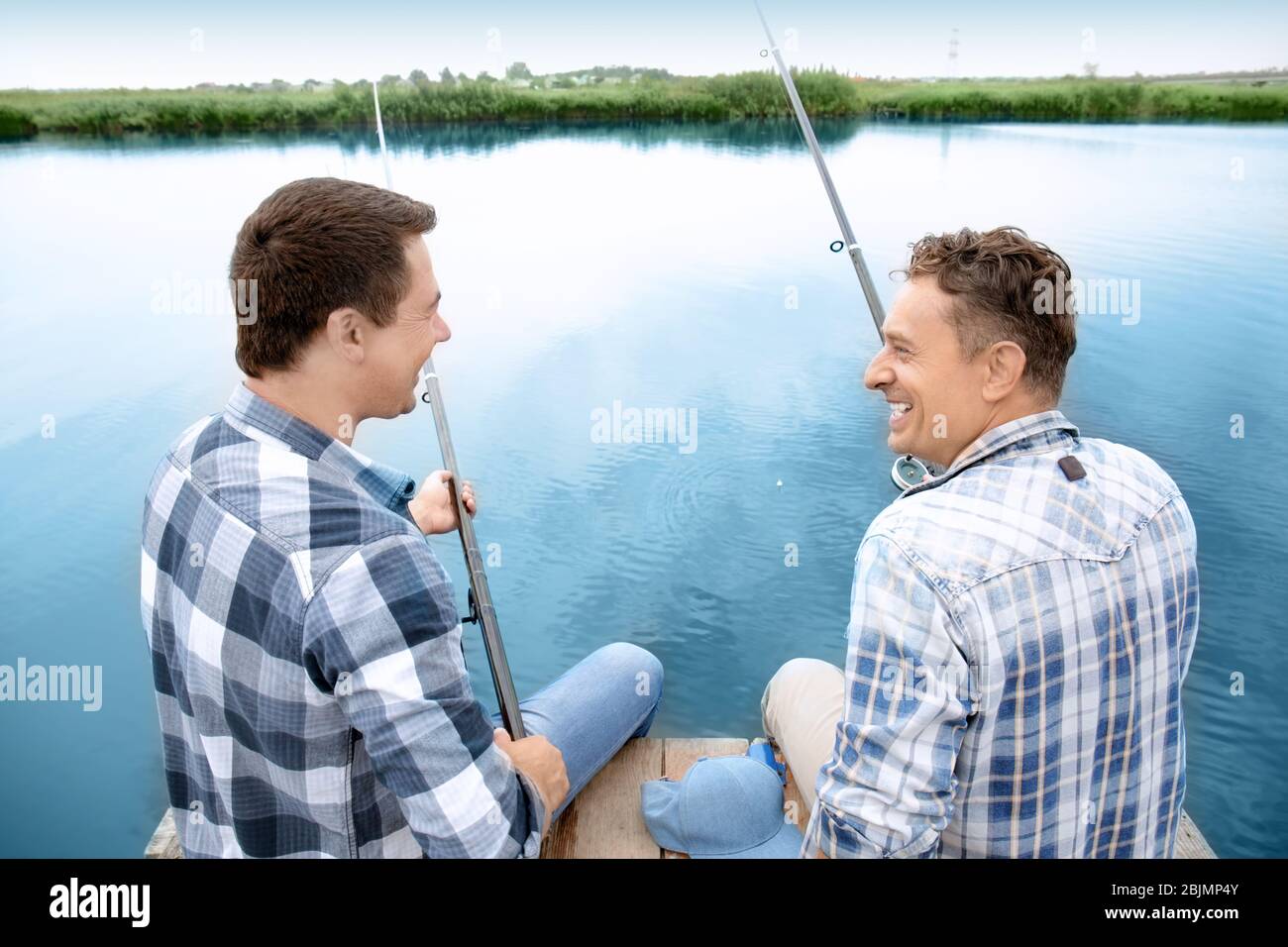 Two men fishing from pier on river Stock Photo - Alamy