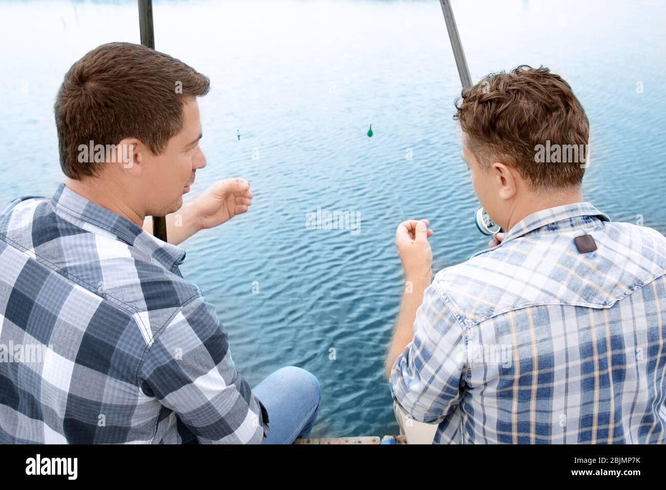 Two men fishing from pier on river Stock Photo - Alamy