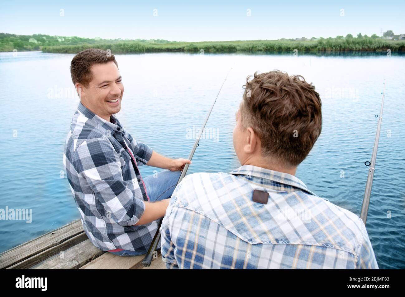 Two men fishing from pier on river Stock Photo - Alamy