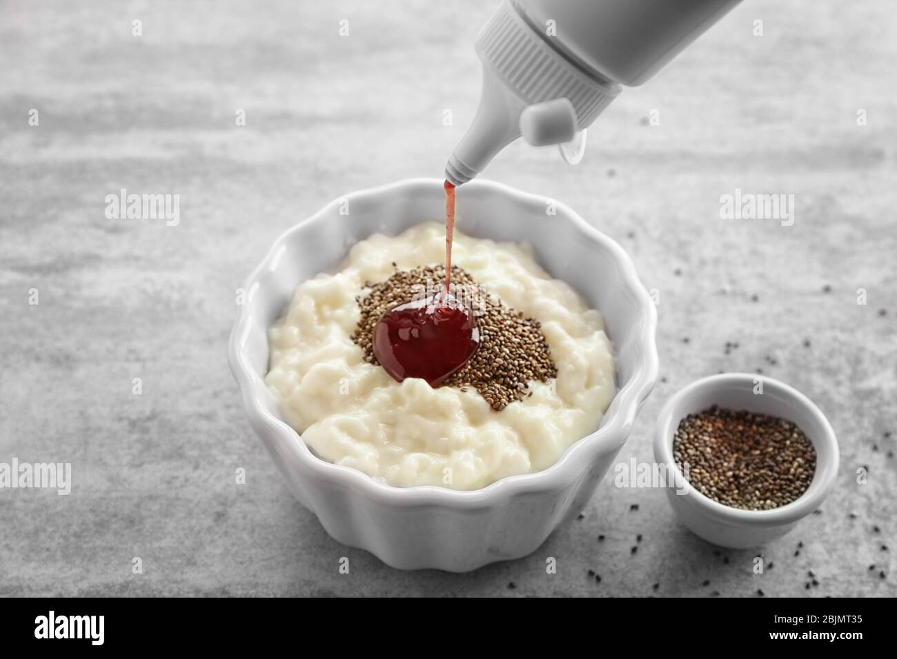 Pouring jam into bowl with pudding and chia seeds on grey table Stock ...