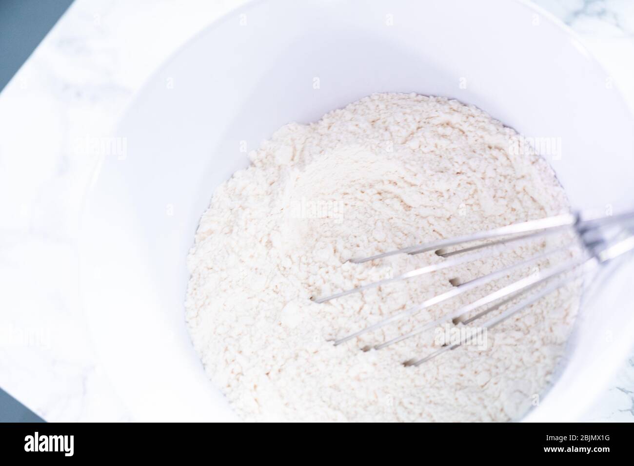 Mixing white flour and other dry ingredients with a whisk in a white ...