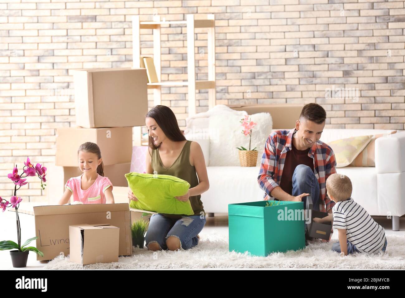 Happy family unpacking cardboard boxes in room at new house Stock Photo ...