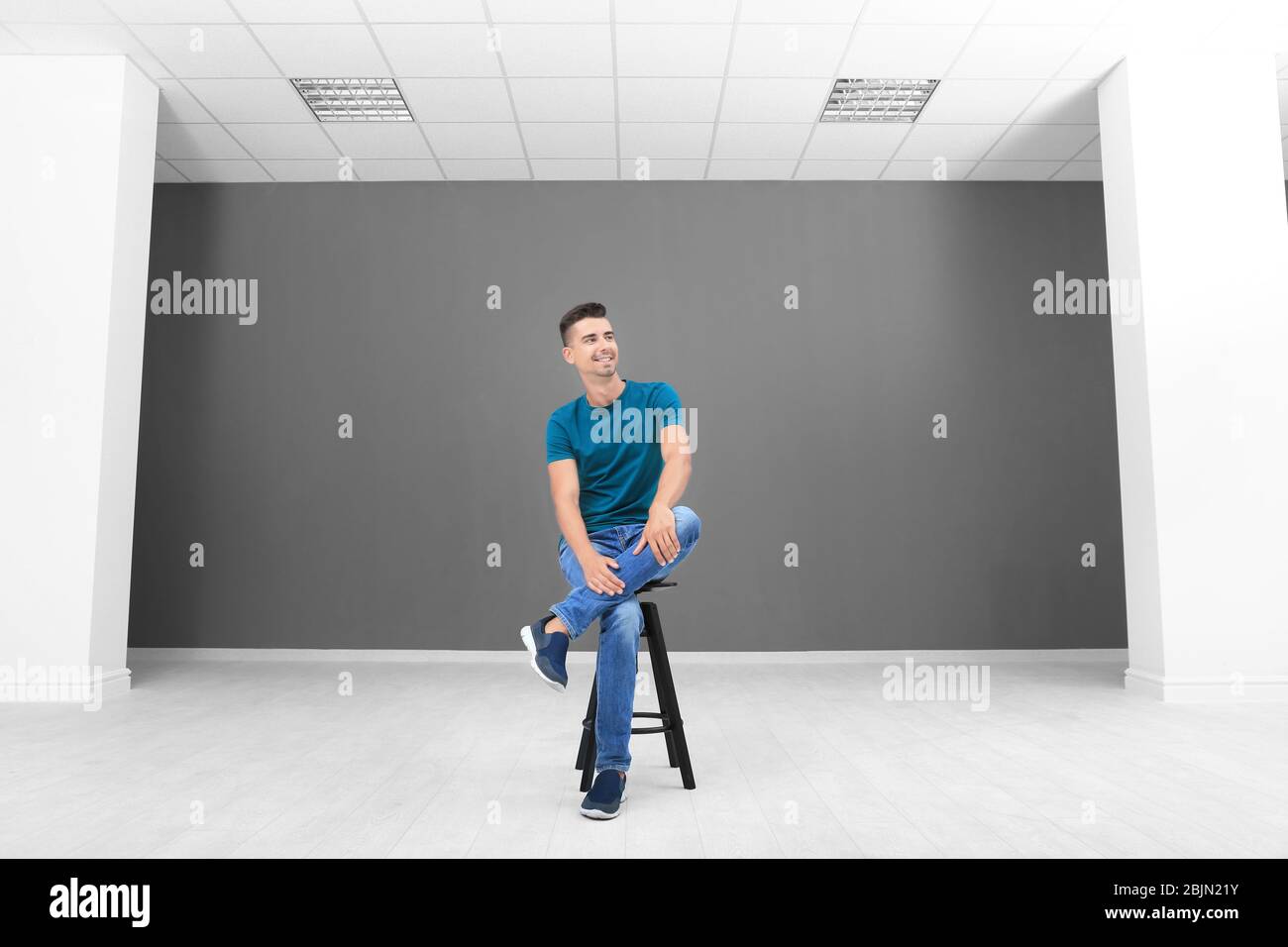 Young man sitting on stool in empty room Stock Photo - Alamy