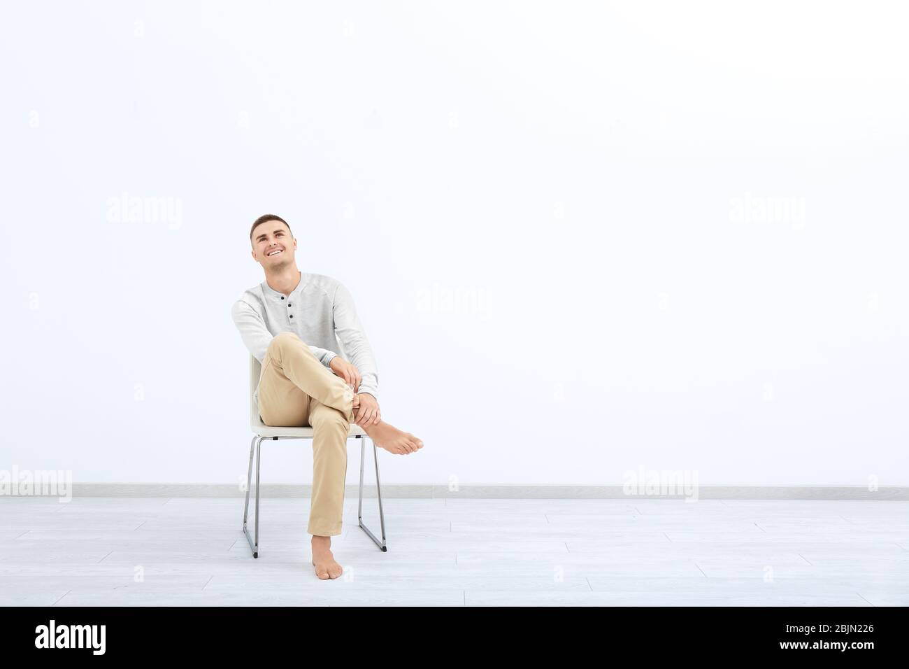 Young man resting on chair against white wall Stock Photo - Alamy