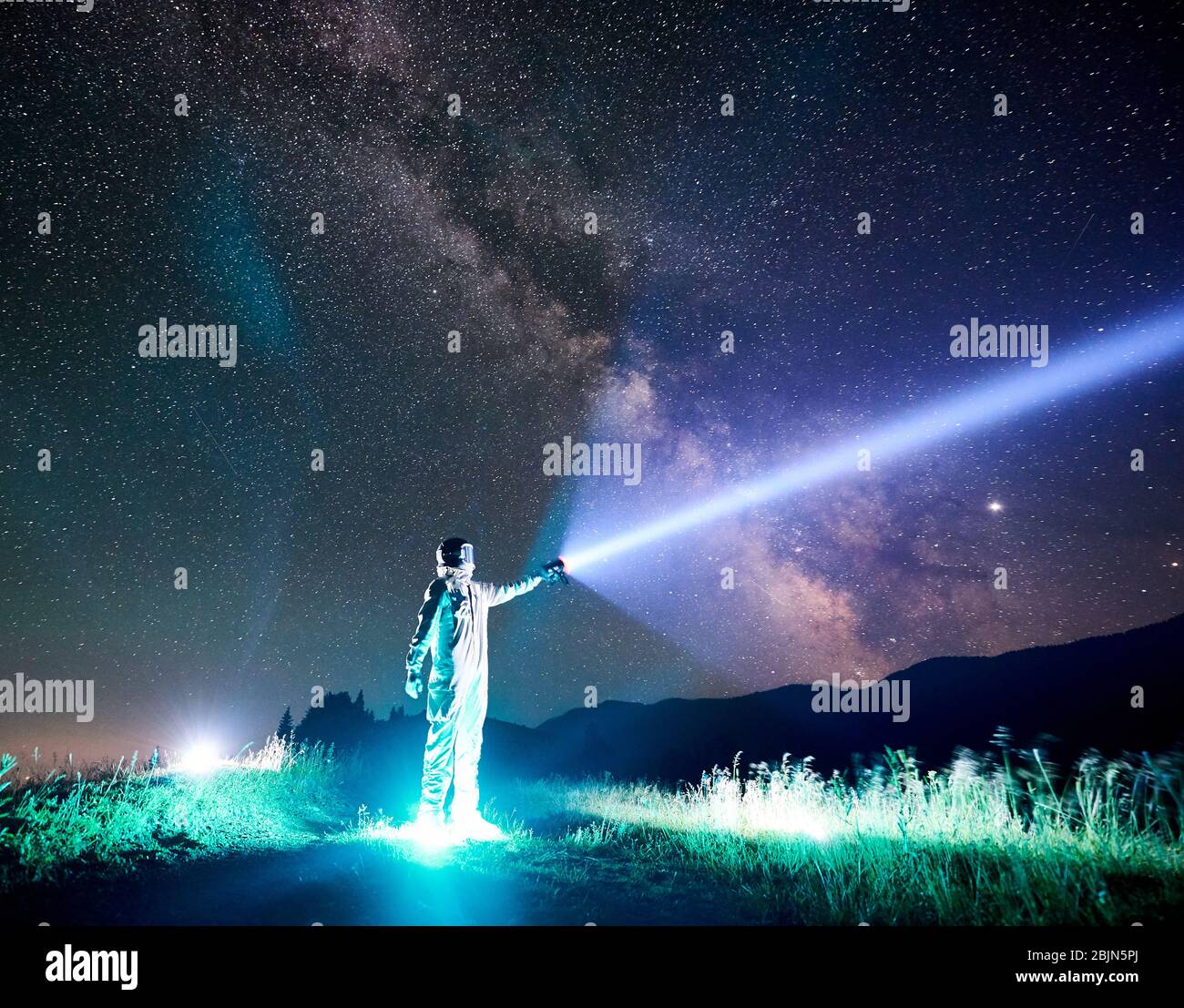 Full length of astronaut illuminating beautiful starry sky with ...