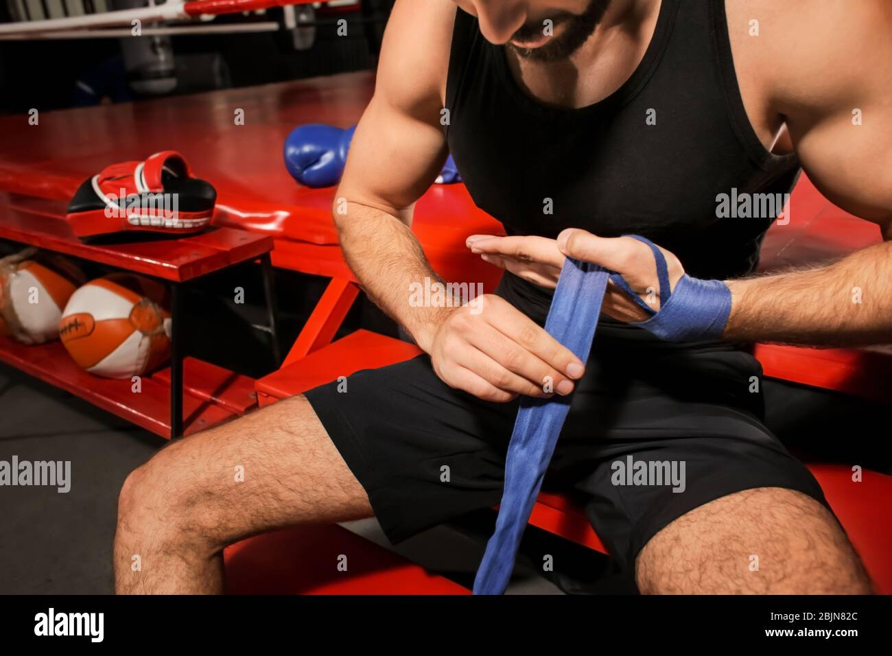 Male boxer applying hand wraps while preparing for training in gym ...