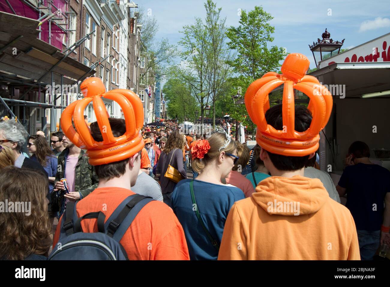 Two guys with inflatable orange crowns stroll through the crowded ...