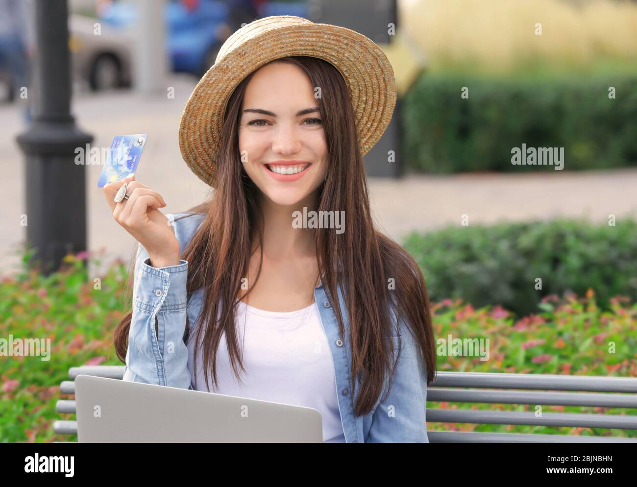 Young woman with laptop and credit card sitting on bench outdoors ...