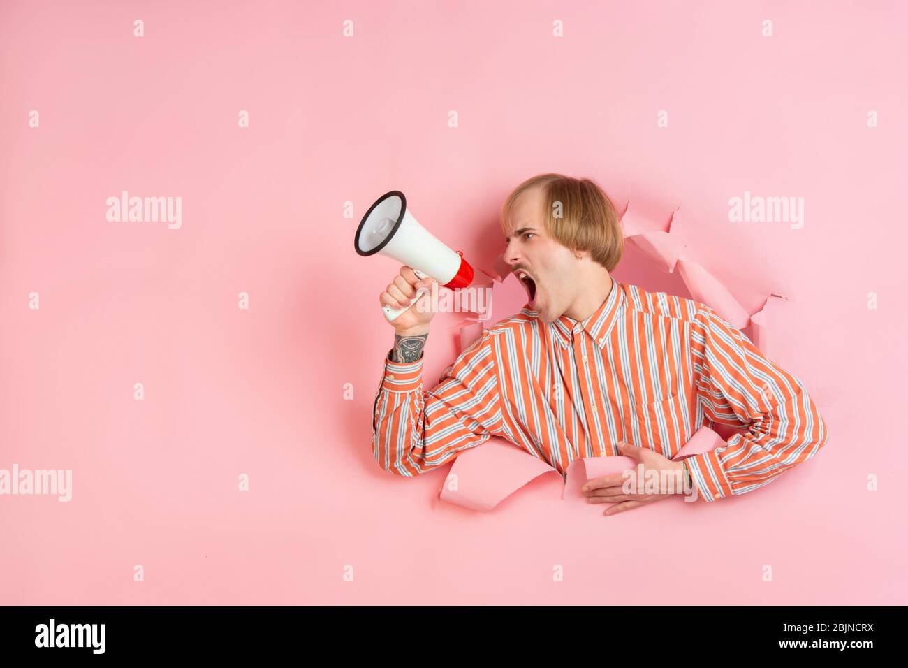 Shouting using speaker. Cheerful caucasian young man poses in torn ...