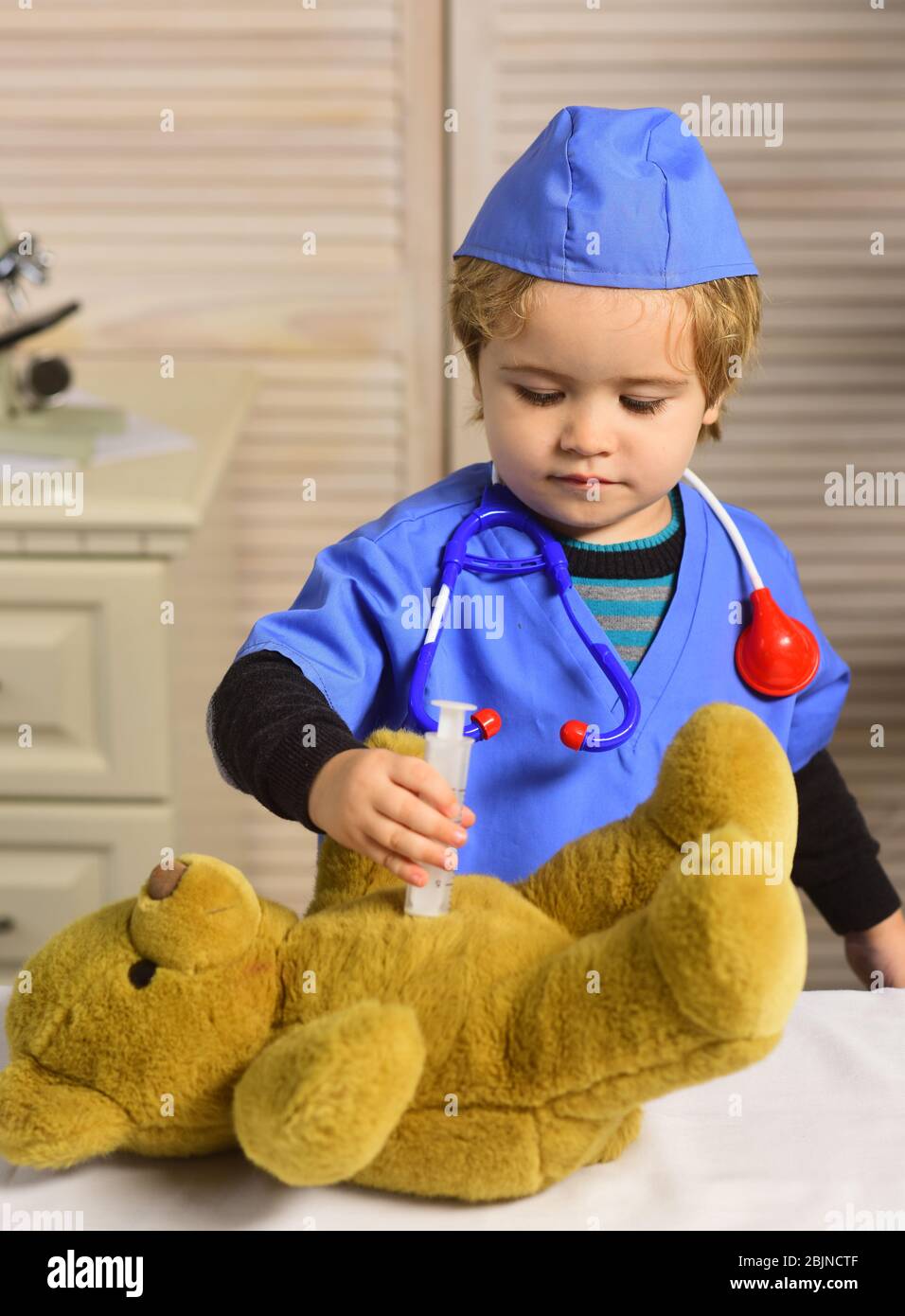 Boy in surgical uniform holds syringe on wooden background. Kid in ...