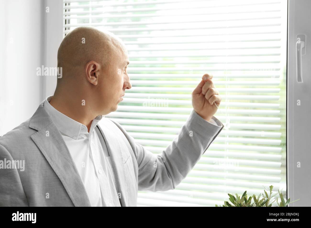 Bald man in jacket standing near window indoors Stock Photo - Alamy