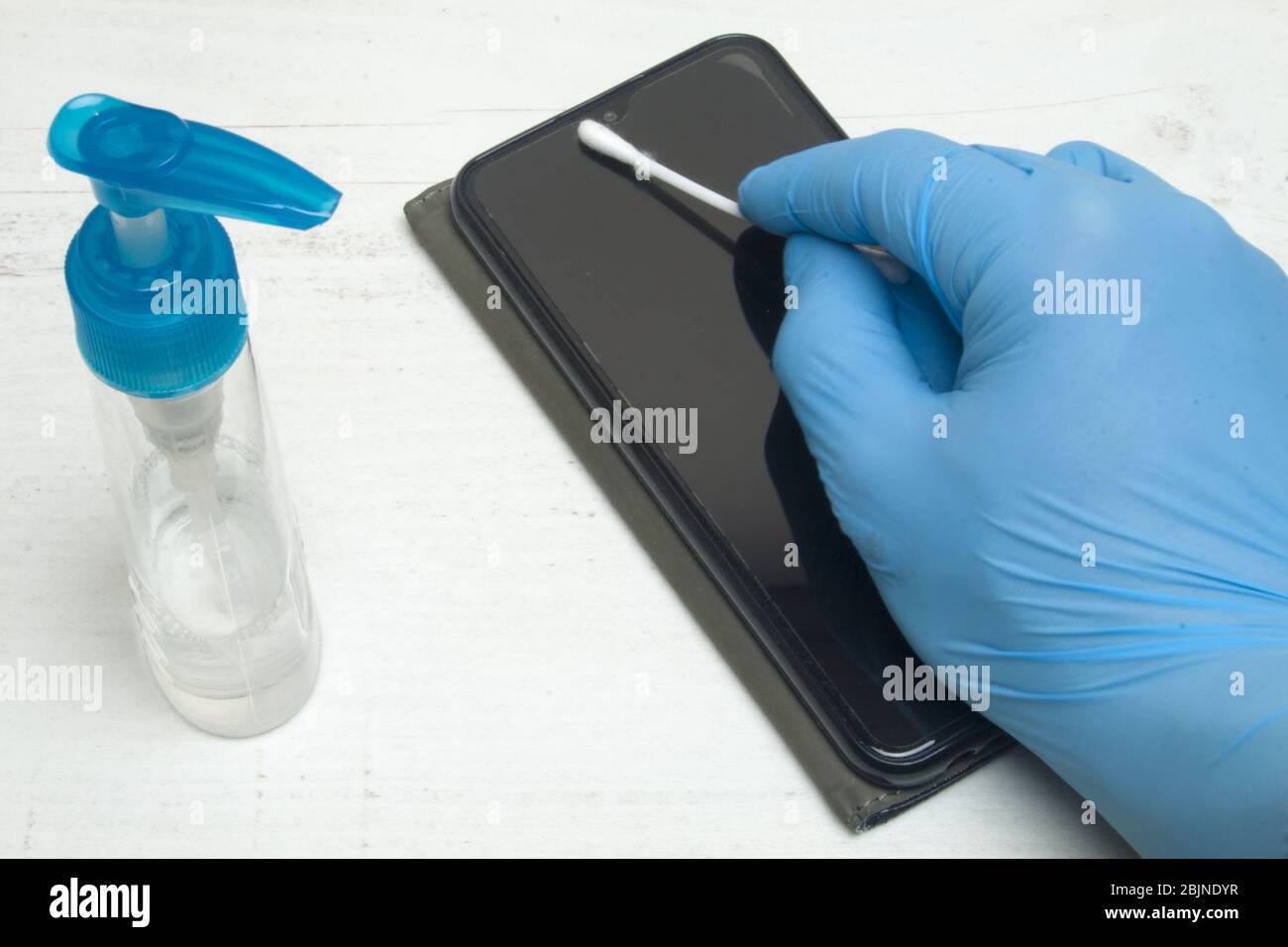 Human hand in a protective glove cleaning smartphone with disinfectant ...