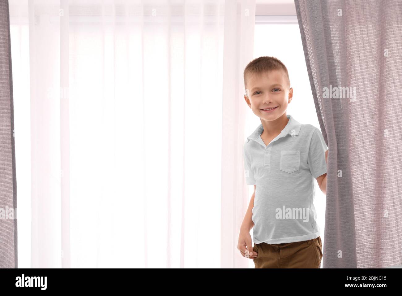 Cute boy standing near window with beautiful curtains indoors Stock ...