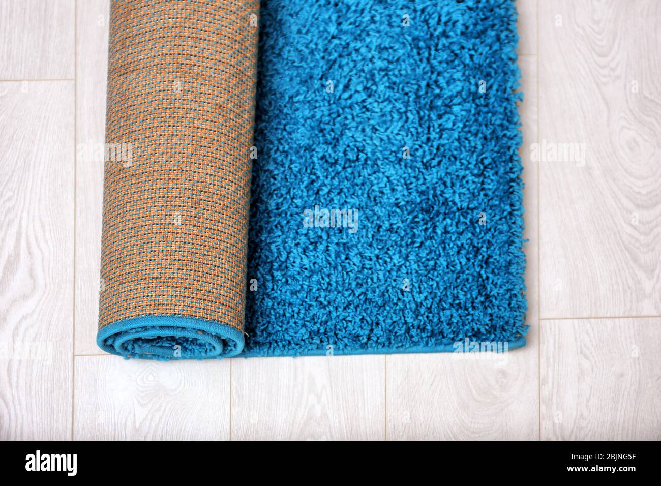 Rolled blue carpet on wooden floor, closeup Stock Photo - Alamy