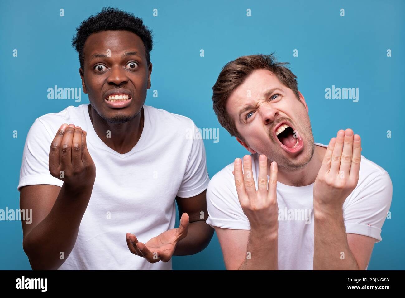 Two friends angry men looking angry showing italian gesture over blue ...