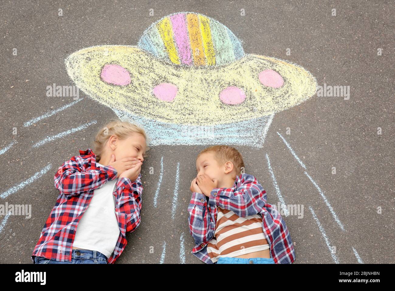Little boy and girl lying near chalk drawing of alien spaceship on ...