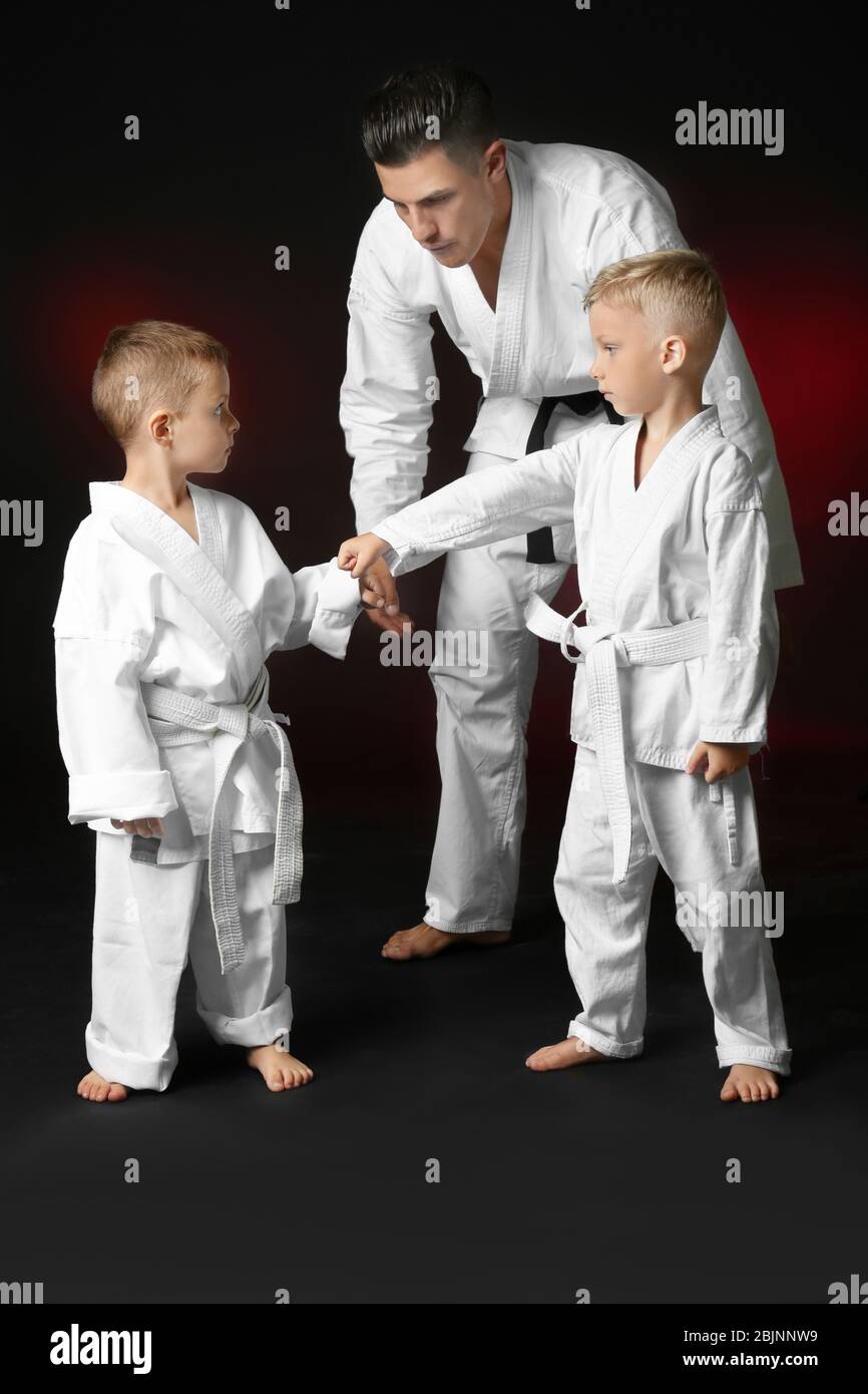 Little children with instructor practicing karate on dark background ...