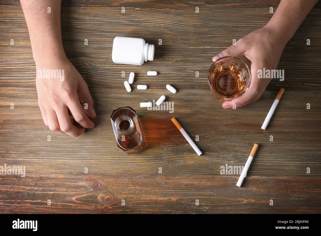 Man sitting at table with cigarettes, drugs and alcohol at wooden table ...