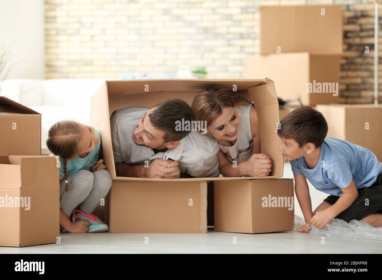 Parents playing with children while unpacking things in new flat Stock ...
