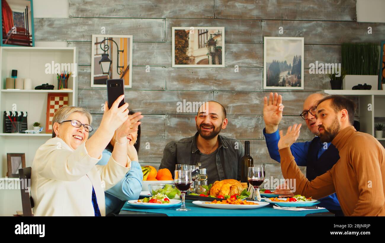 Cheerful family laughing while video call chatting from phone at dinner ...