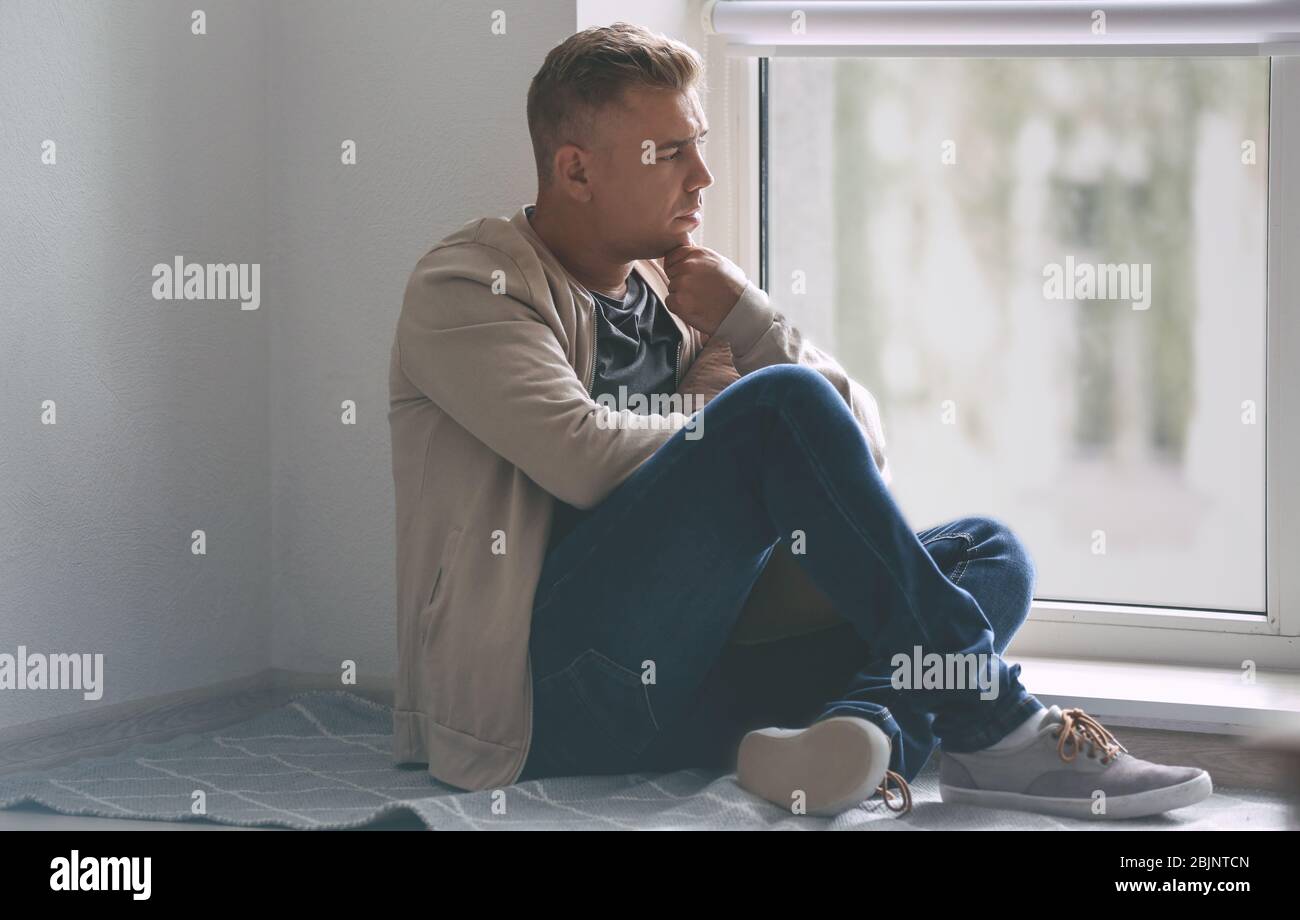 Depressed man near window at home Stock Photo - Alamy