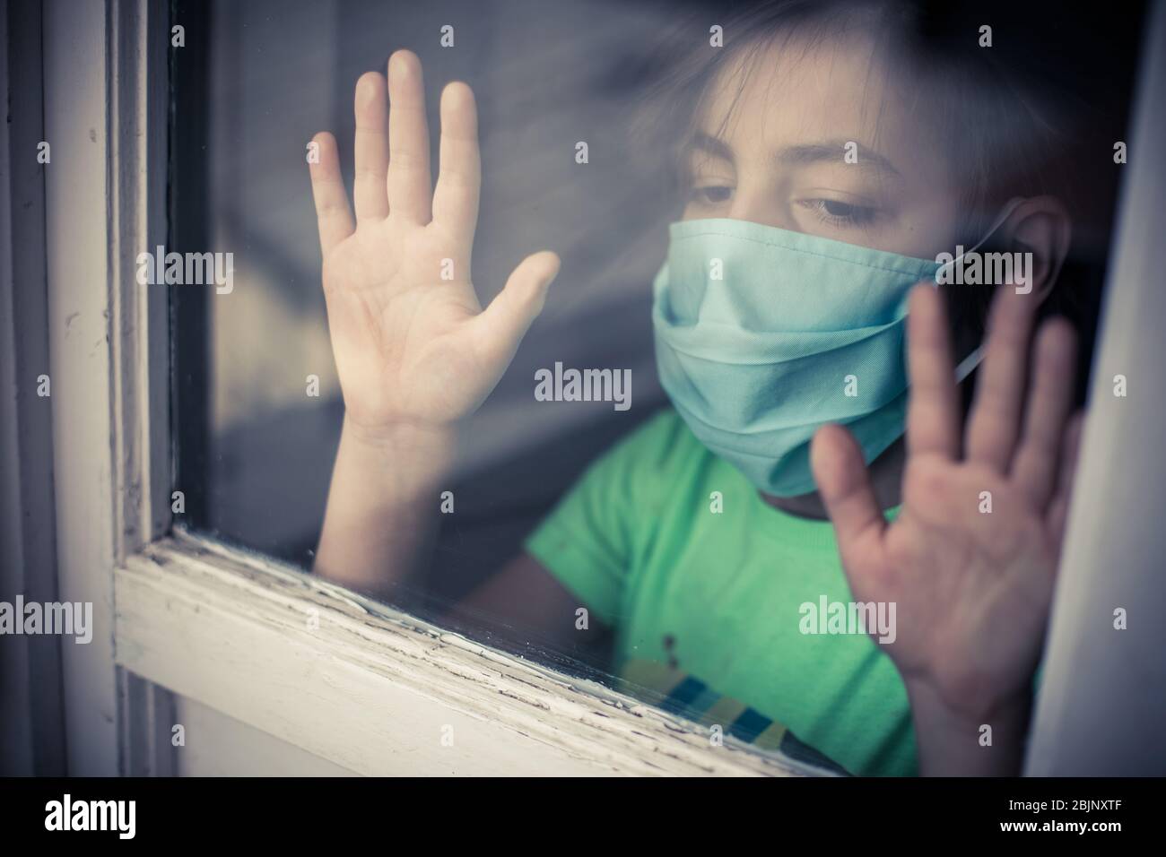 Image of a kid wearing a surgical mask, isolated at home, behind a ...