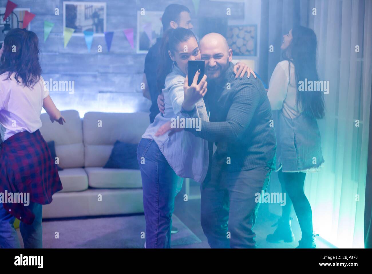 Cheerful bald man taking a selfie with his girlfriend at the party ...