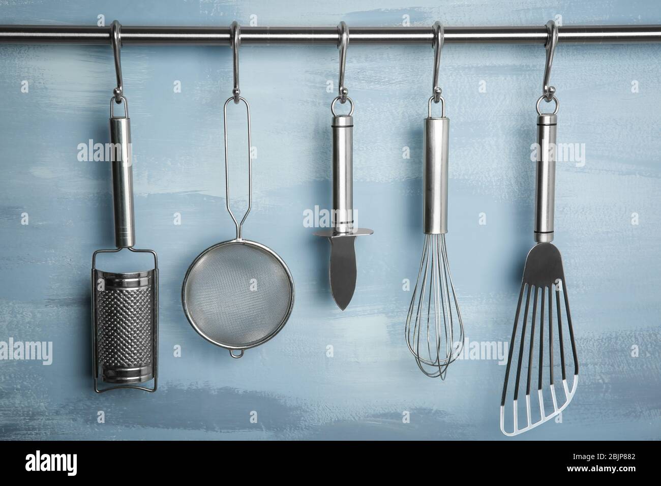 Metal kitchen utensils hanging on rack against color wall Stock Photo ...