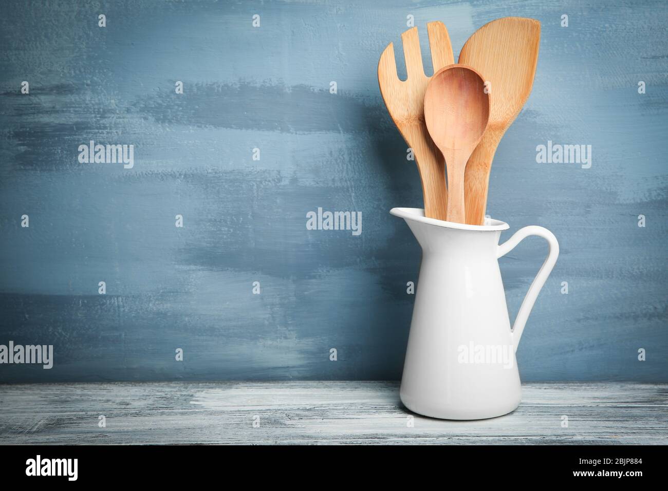 Wooden kitchen utensils in jug on table against wall Stock Photo - Alamy