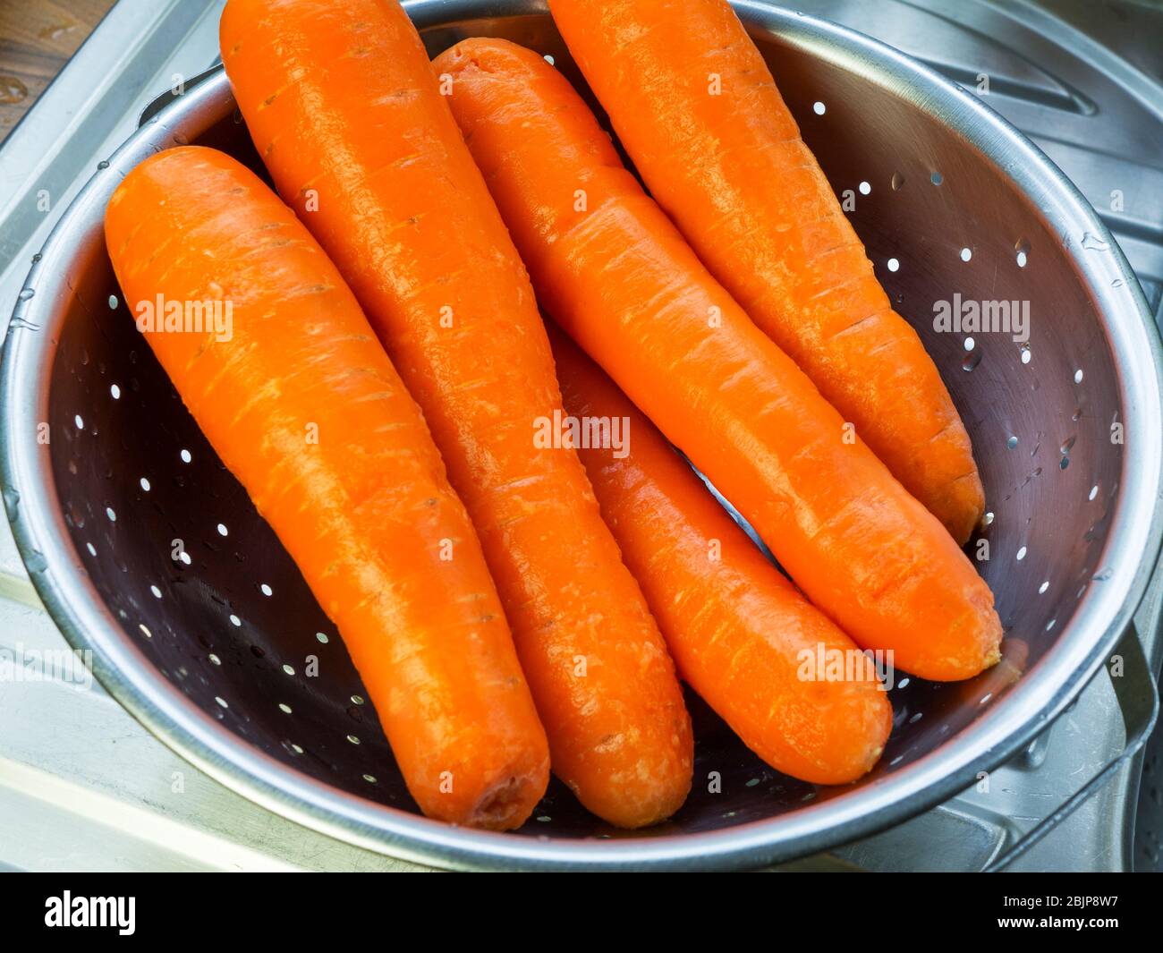 Five washed orange carrots in a stainless steel colander on a kitchen ...