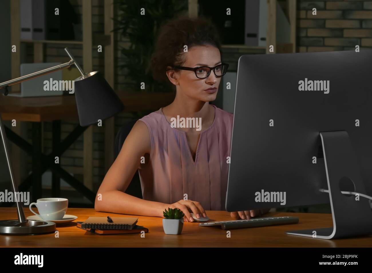 Attractive young woman working late in office Stock Photo - Alamy