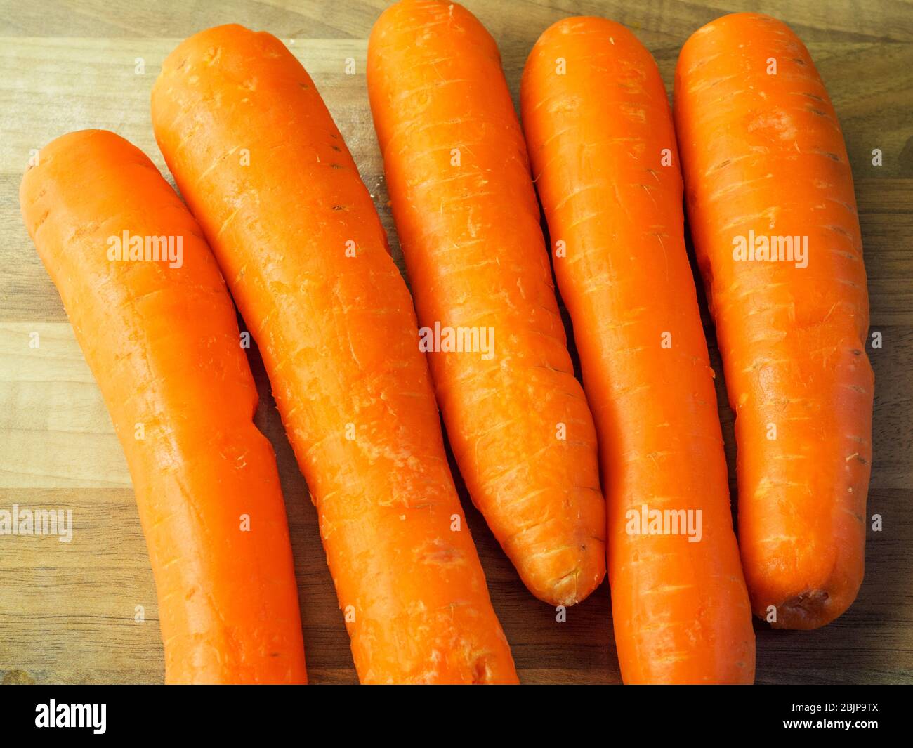 Five fresh orange carrots on a wood block kitchen worktop Stock Photo ...
