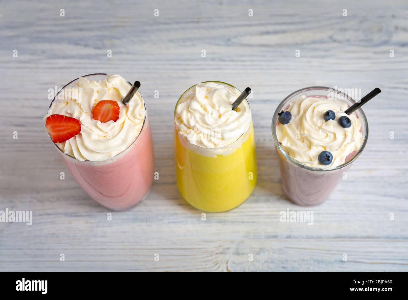 Different milkshakes in glasses on wooden background Stock Photo - Alamy