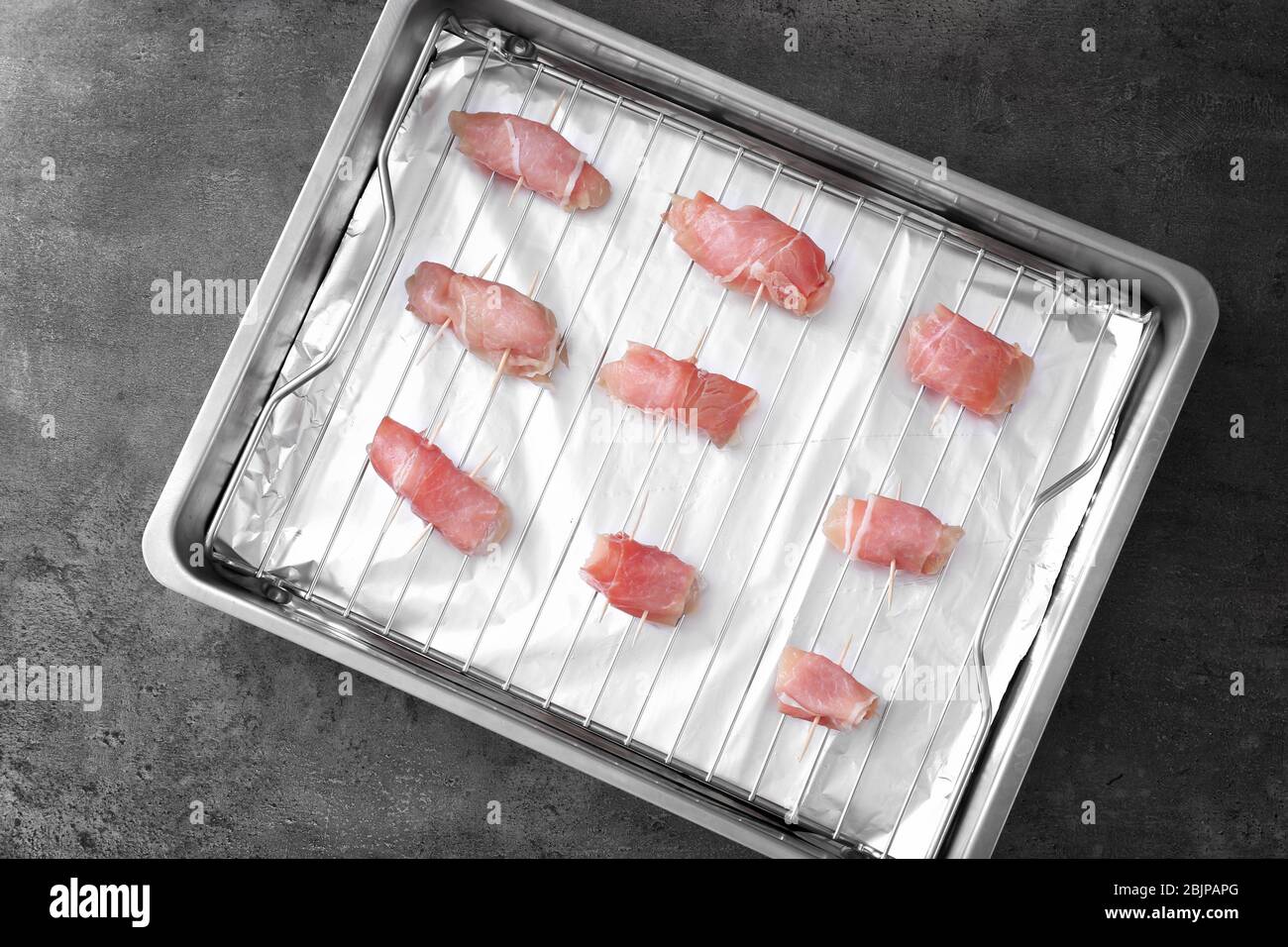Baking grid with raw bacon wrapped chicken on table Stock Photo - Alamy
