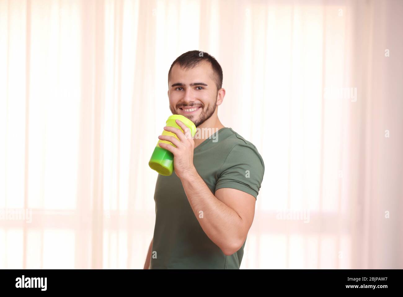 Sporty young man drinking protein shake on light background Stock Photo ...