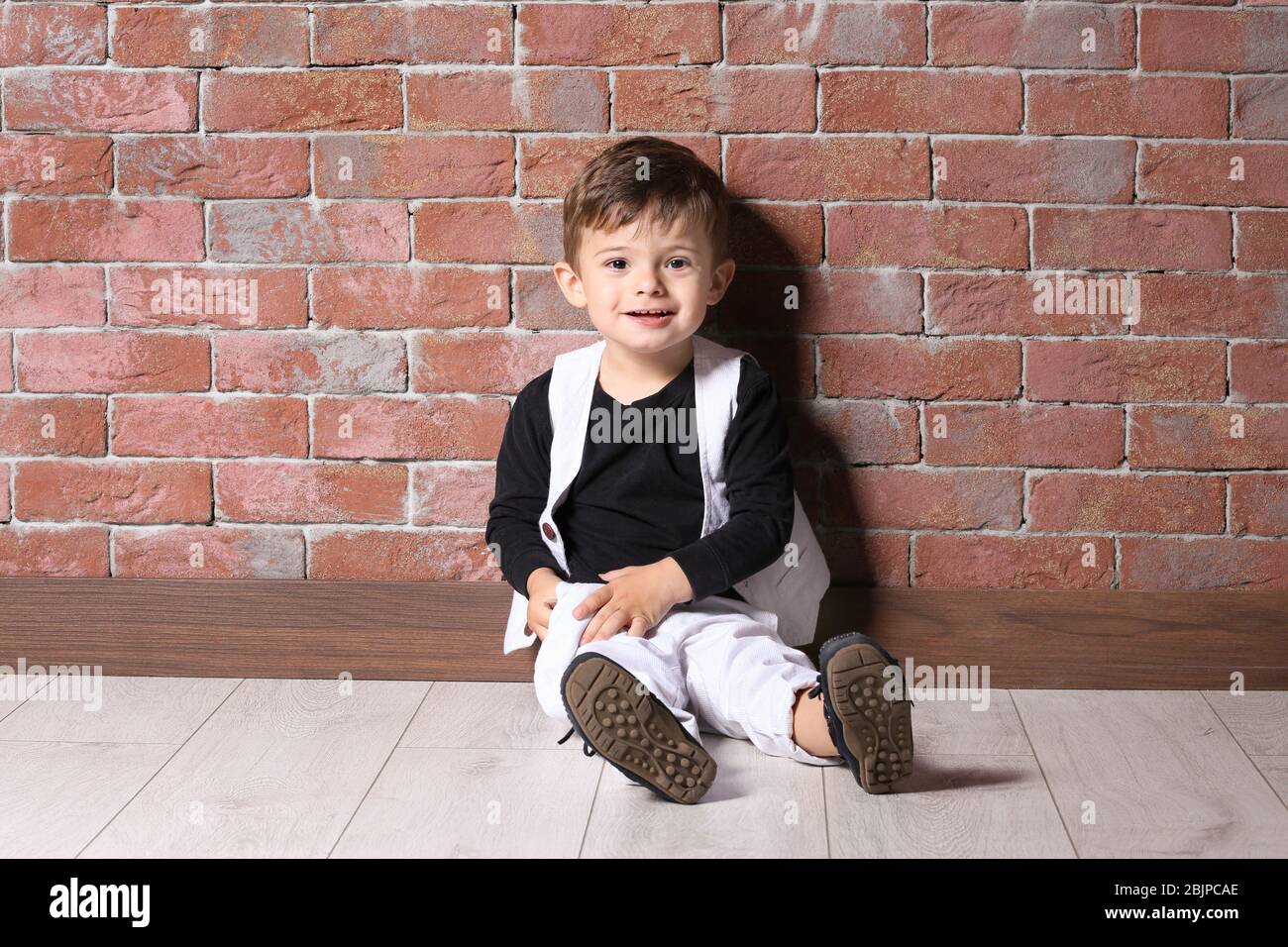Adorable little boy sitting on floor near brick wall Stock Photo - Alamy
