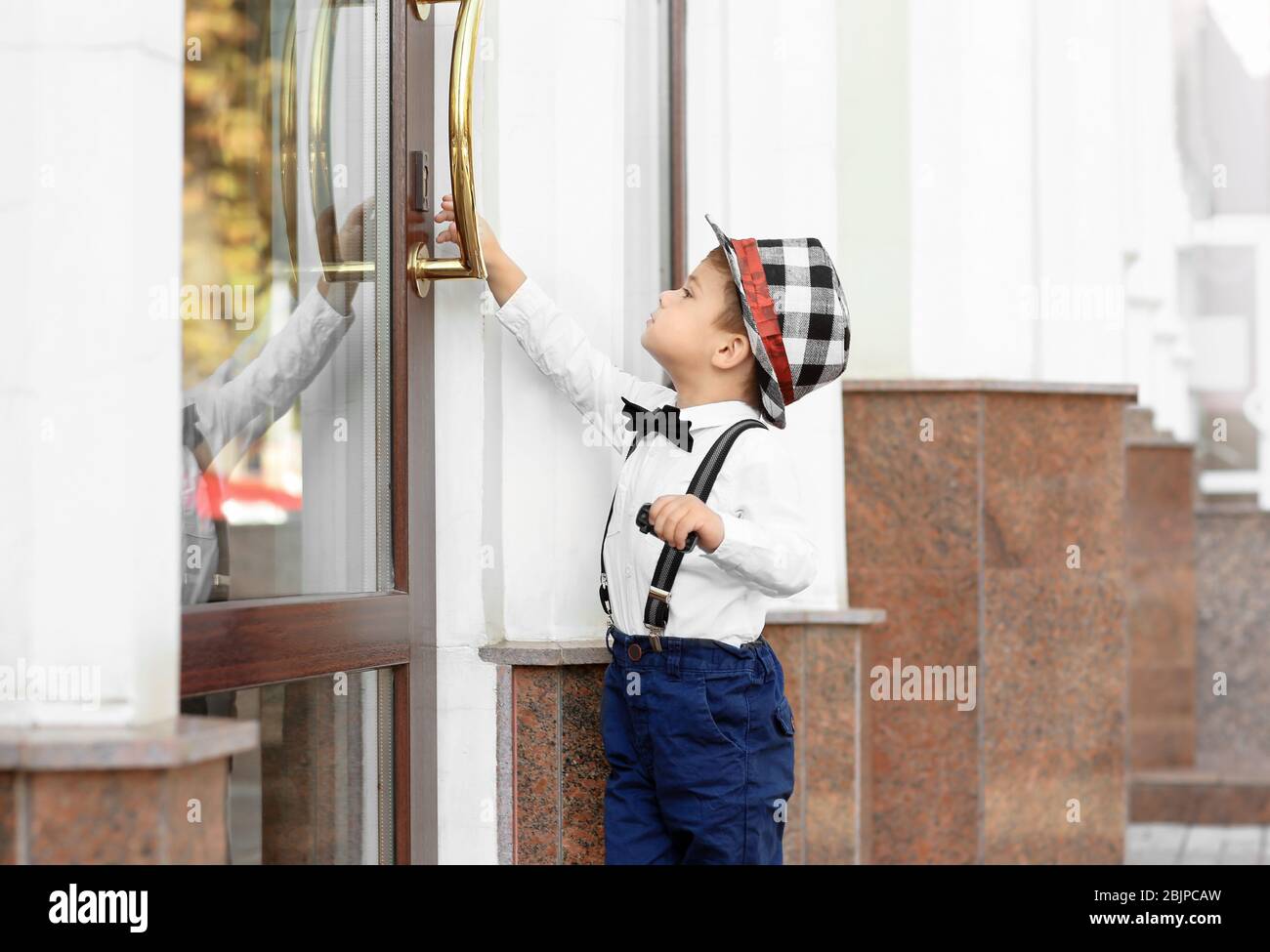 Adorable little boy standing near building entrance outdoors Stock ...