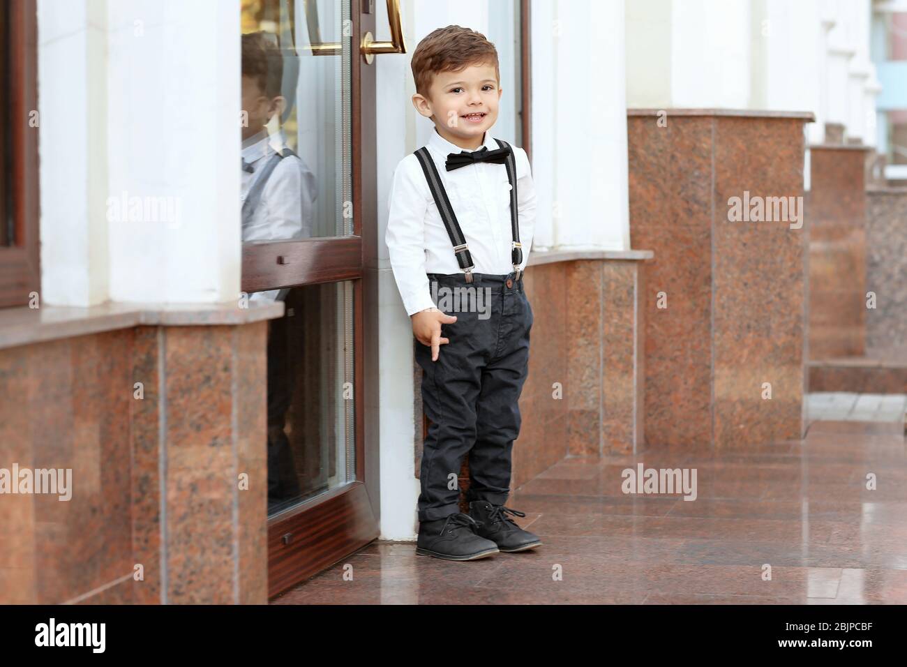 Adorable little boy standing near building entrance outdoors Stock ...
