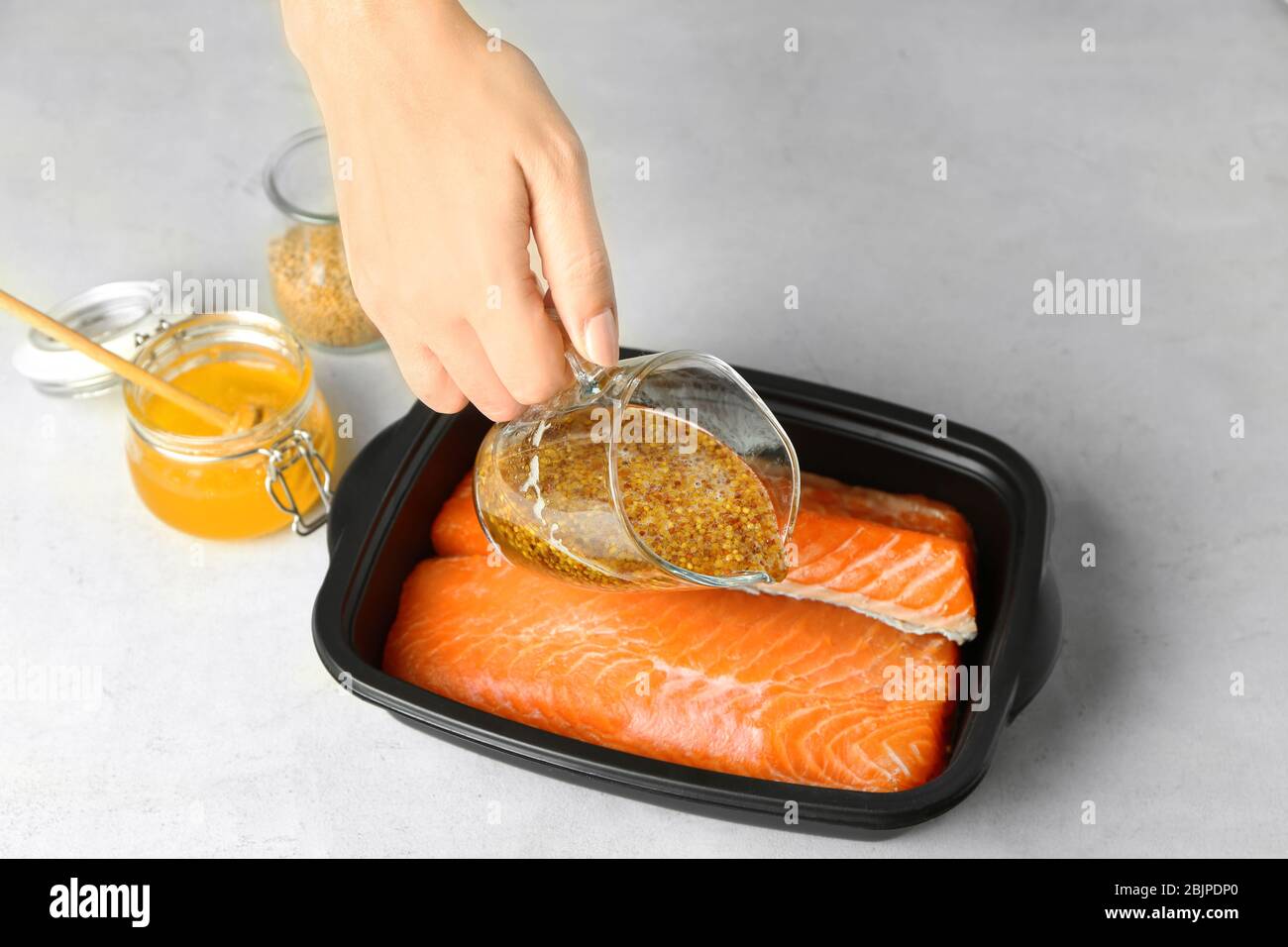 Woman preparing salmon fillet with honey mustard marinade in dish Stock ...