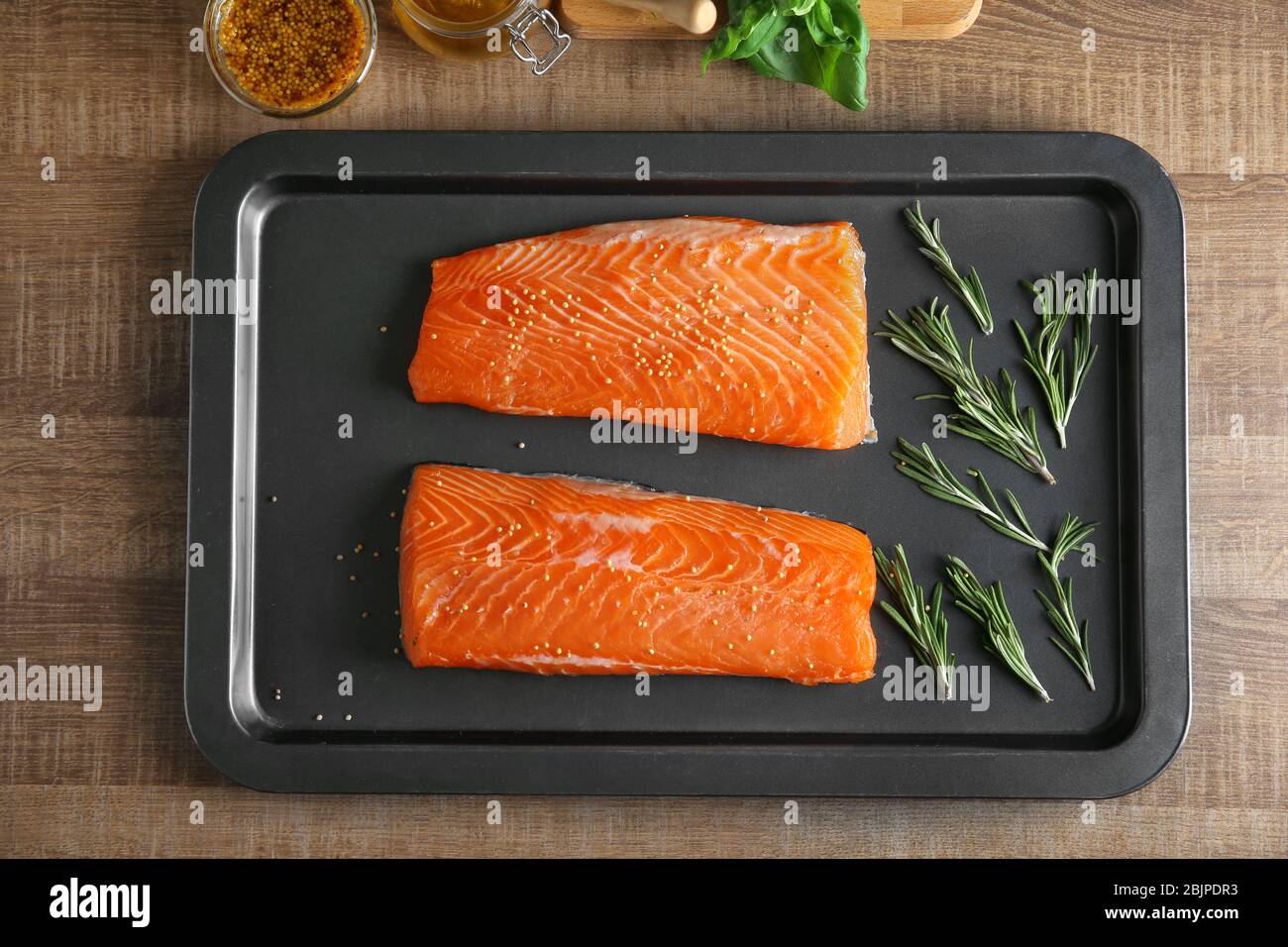 Baking sheet with salmon fillet in honey mustard marinade on table ...