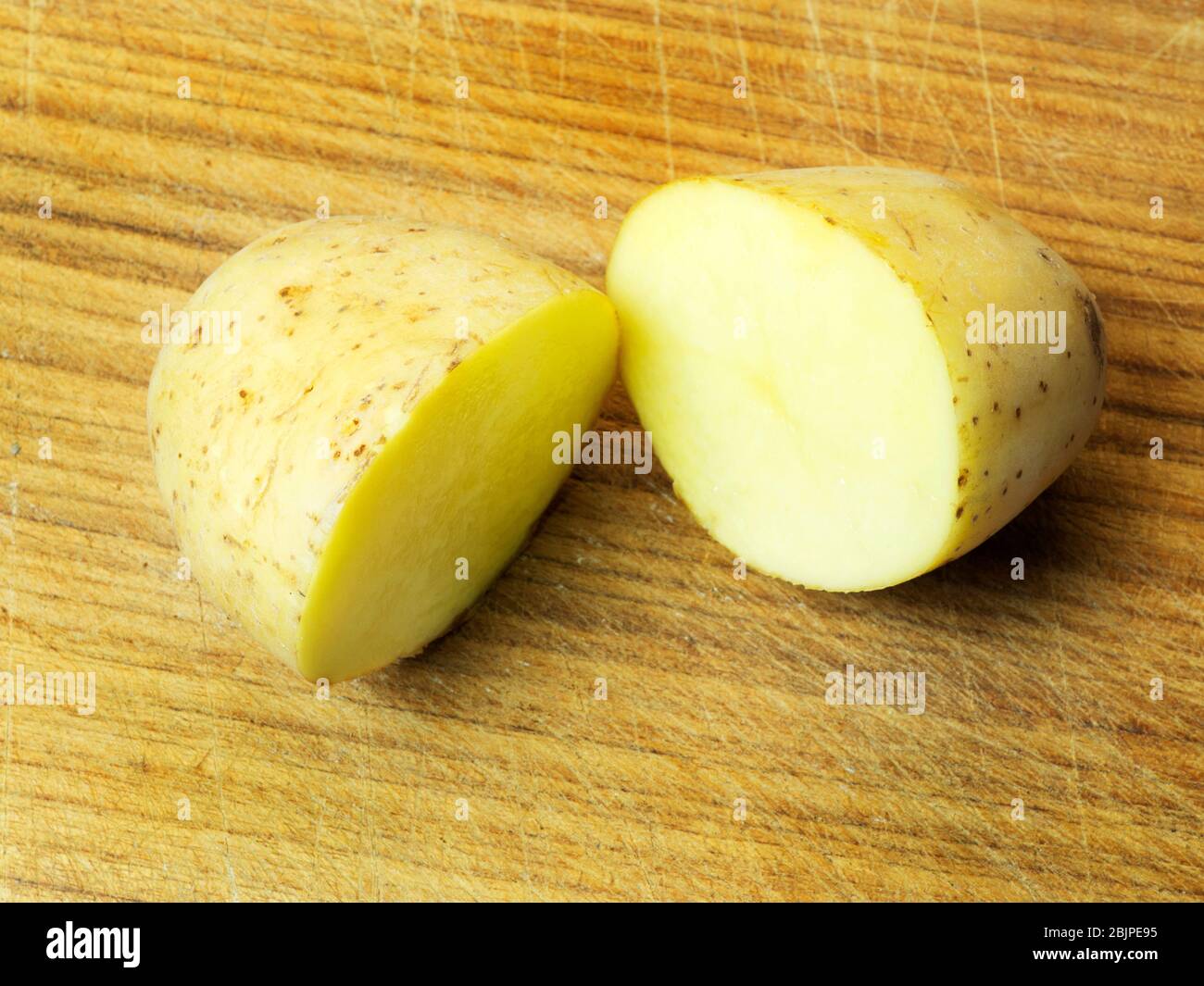 One white potato with skin on cut in half on a wooden chopping board ...