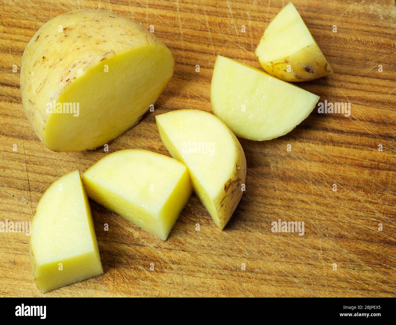 A half white potato and five potato pieces with skin on on a wooden ...