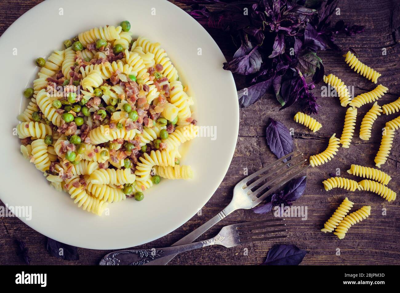 Fusilli with prosciutto and green pease on old wooden background ...