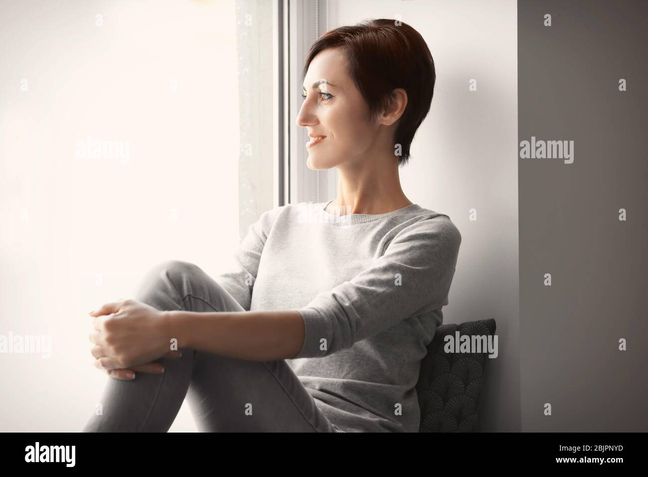 Beautiful mature woman sitting near window at home Stock Photo - Alamy