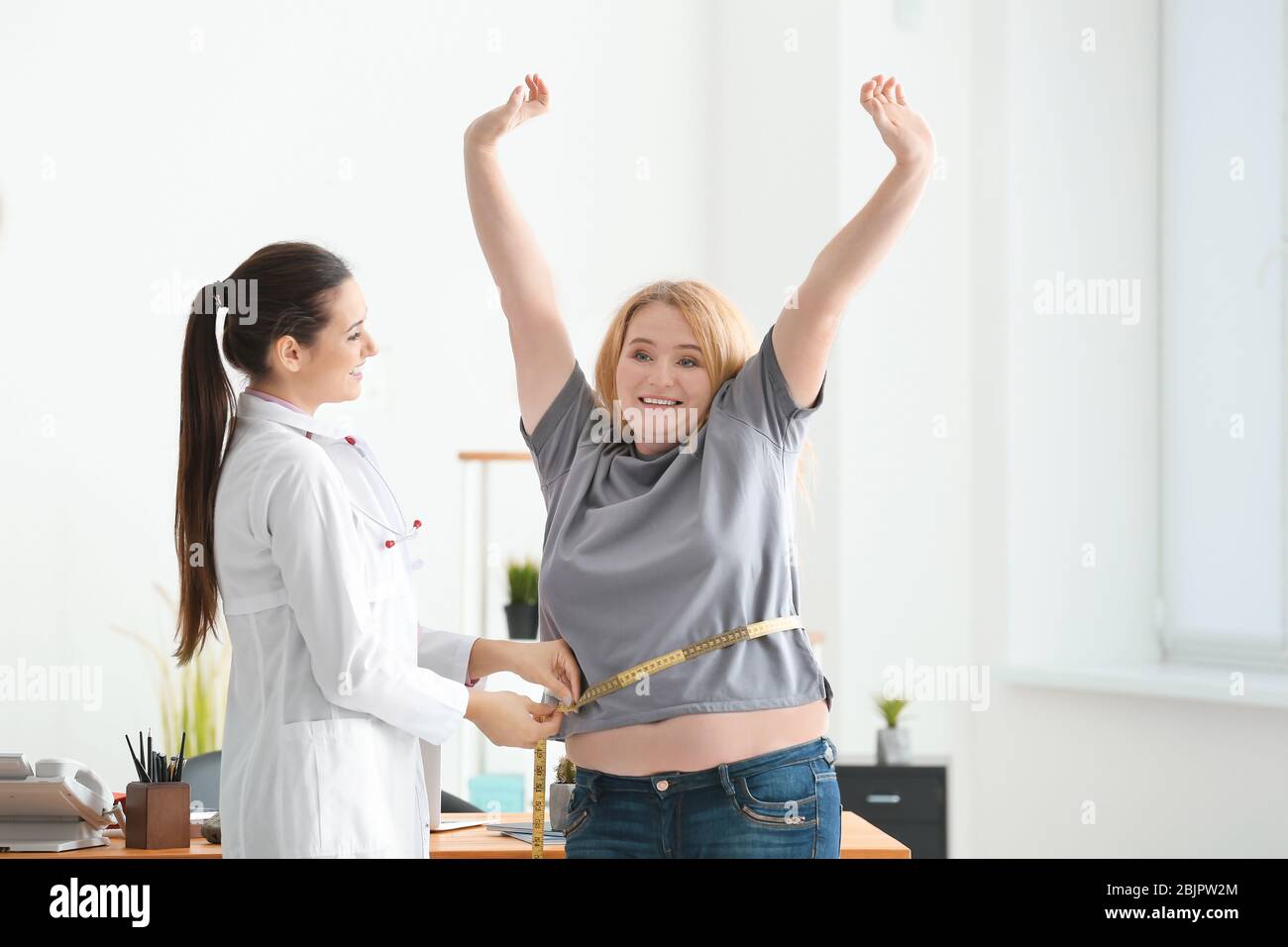 Young female doctor measuring waist of overweight woman with centimeter ...