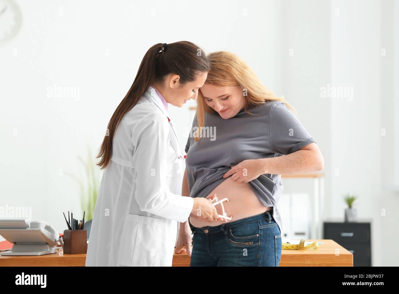 Young female doctor measuring fat layer of overweight woman with ...